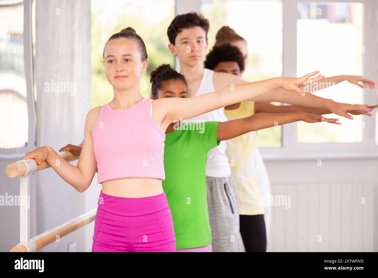 Teen girl mastering second ballet position at barre at group class ...