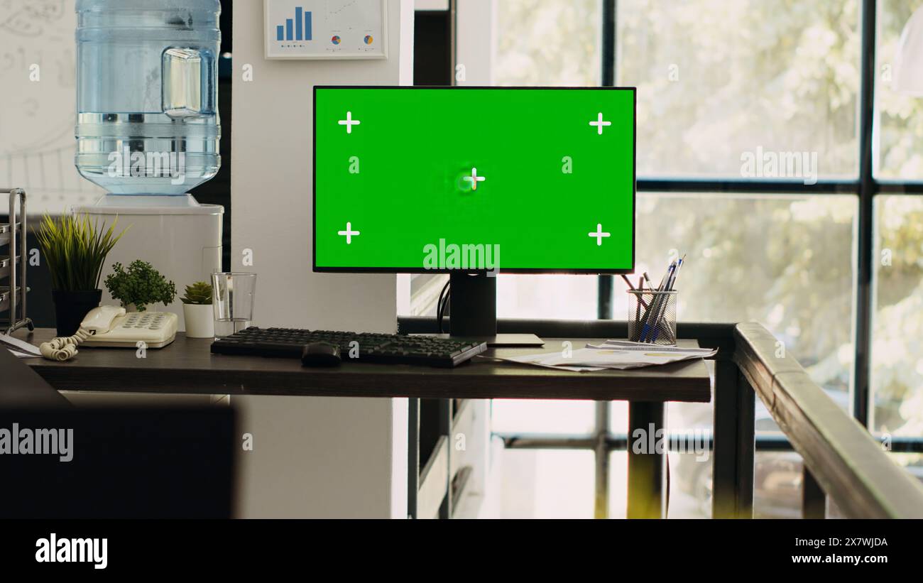 Modern coworking space with monitor showing isolated greenscreen, blank chromakey screen on ...
