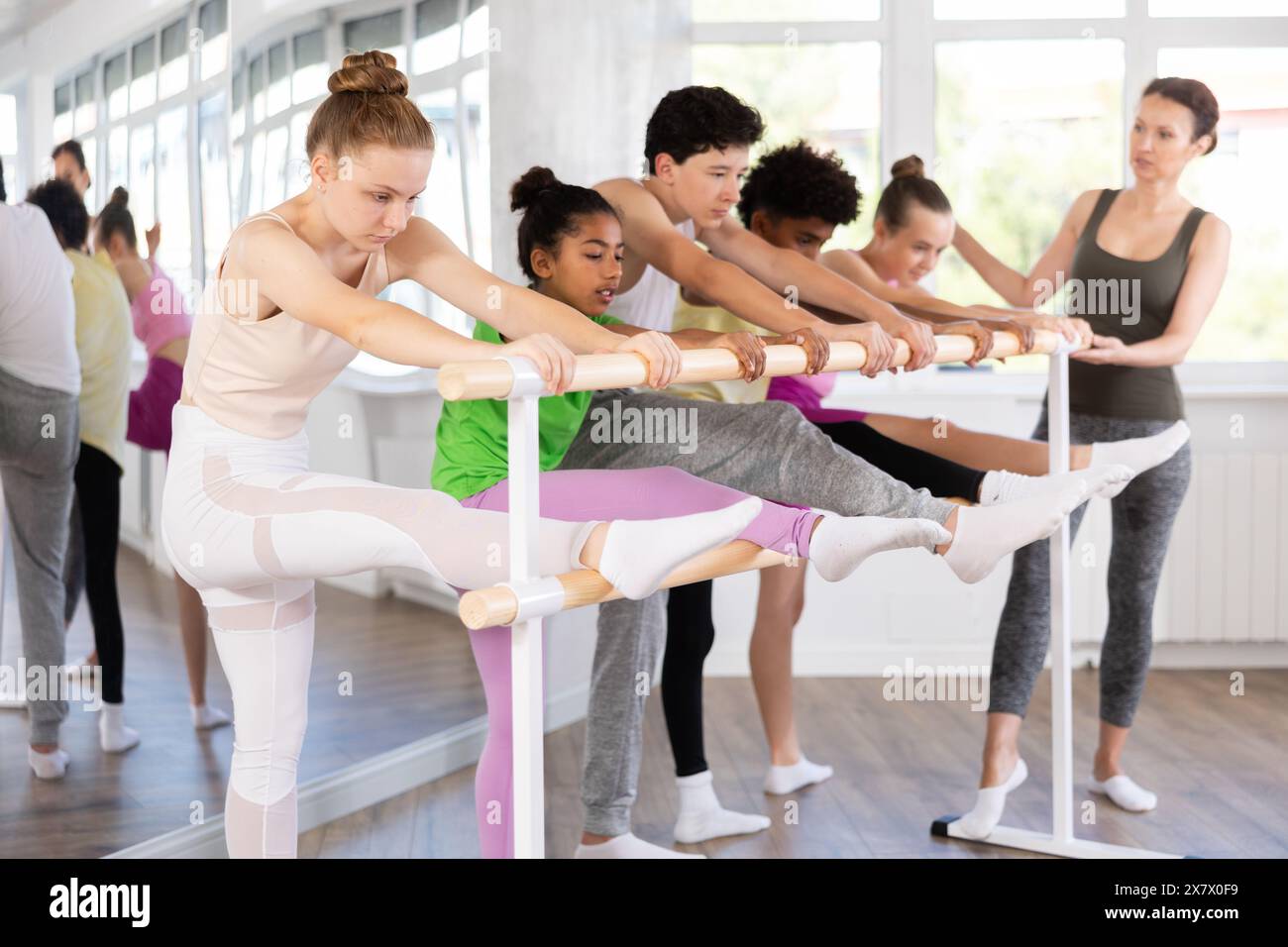 Teenage girl doing leg stretching exercise holding by ballet barre ...