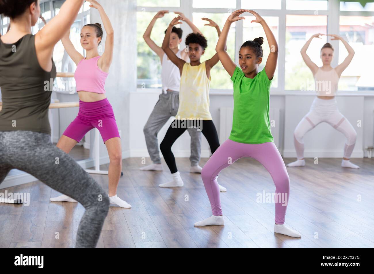Thin teenage girl practicing plie position of ballet standing in row ...