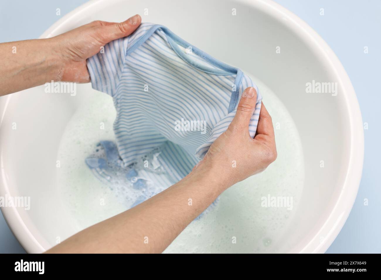 Woman washing baby clothes in basin on light blue background, closeup ...