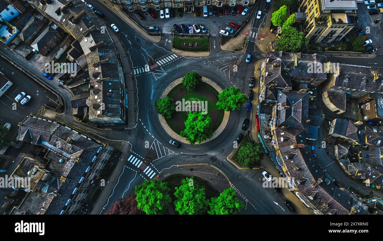Aerial view of a roundabout with green trees in the center, surrounded by buildings and roads ...