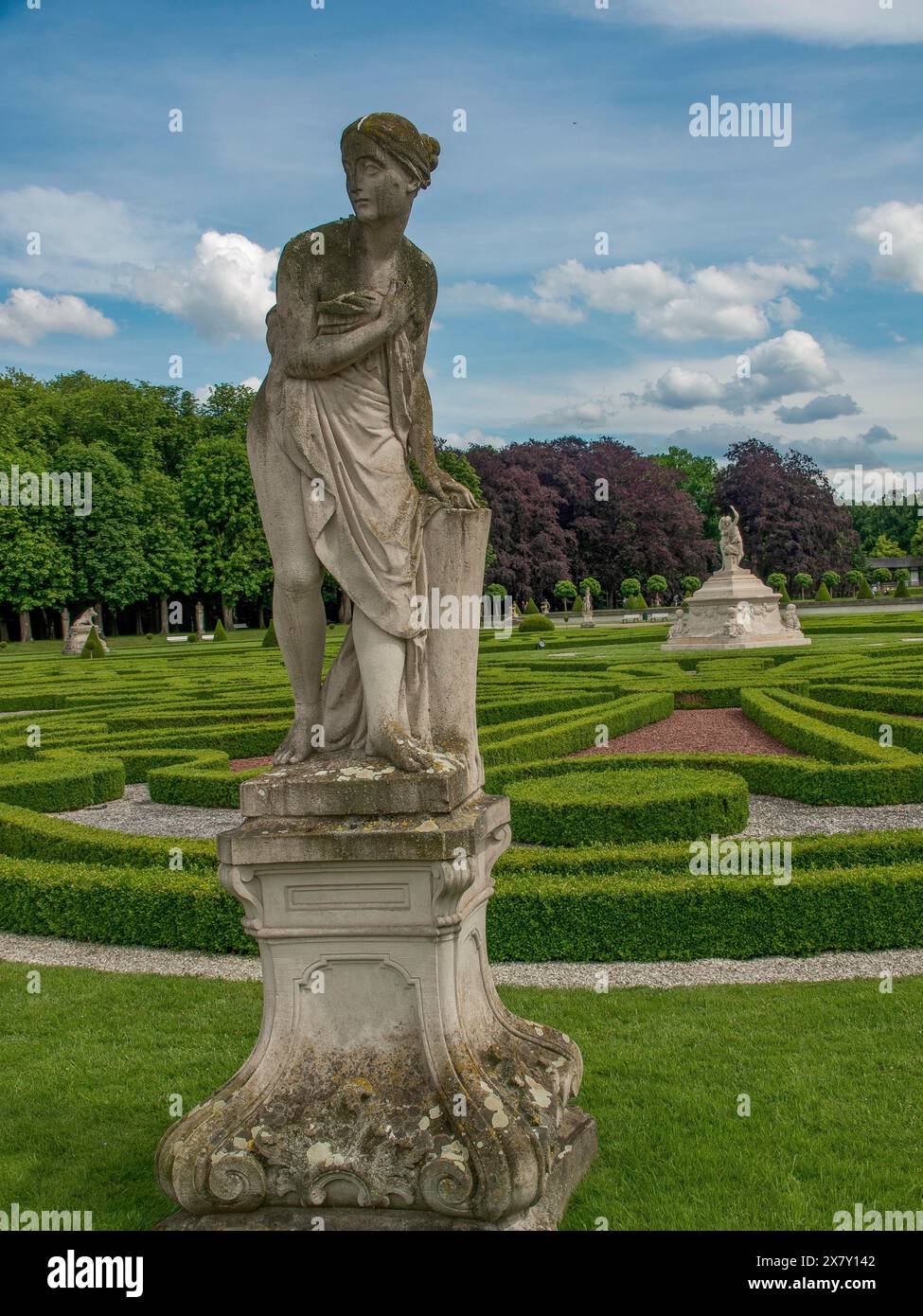 Stone statue of a woman in a well-kept baroque garden with symmetrical ...