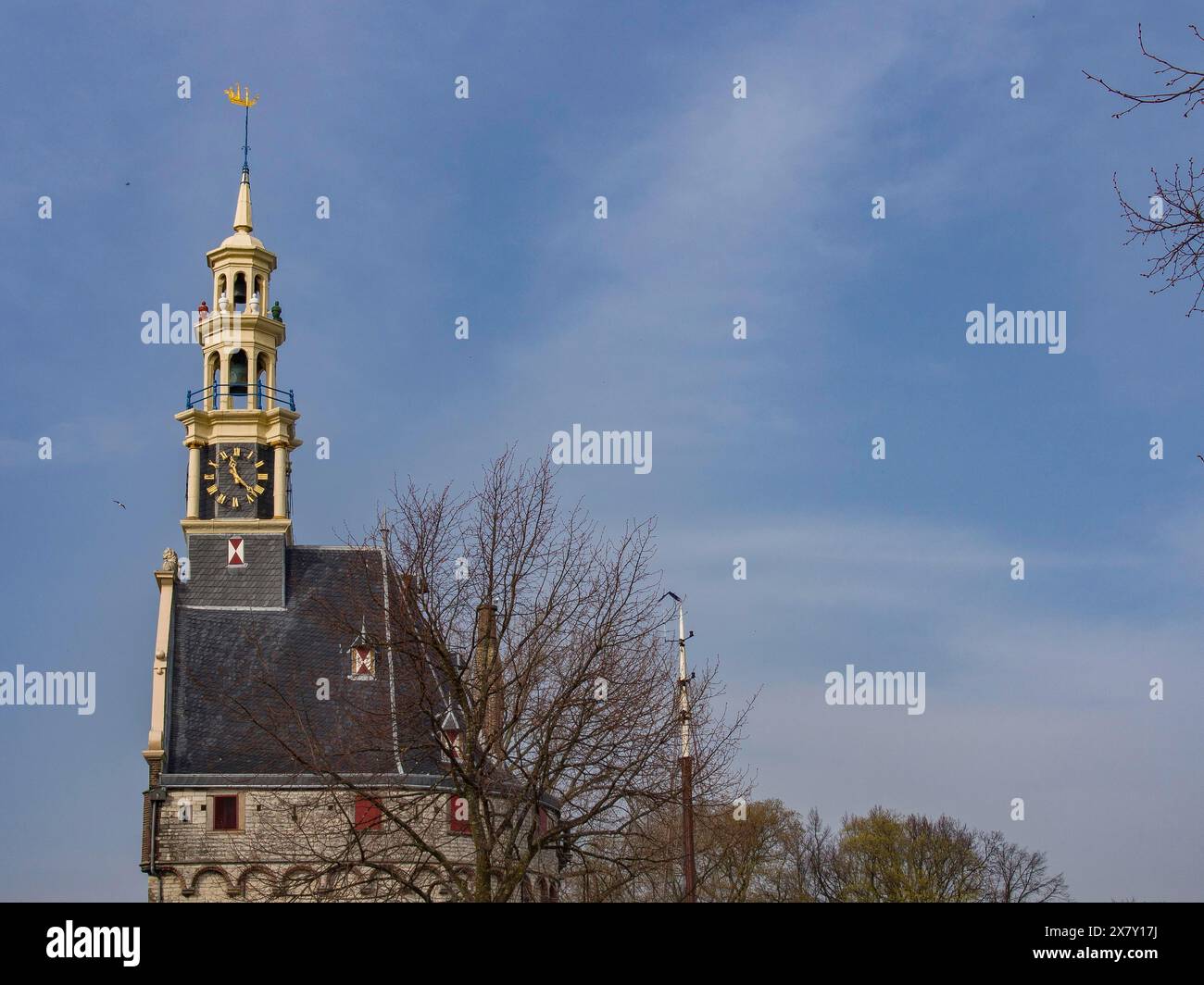 Historic stone clock tower surrounded by trees in front of a blue sky ...