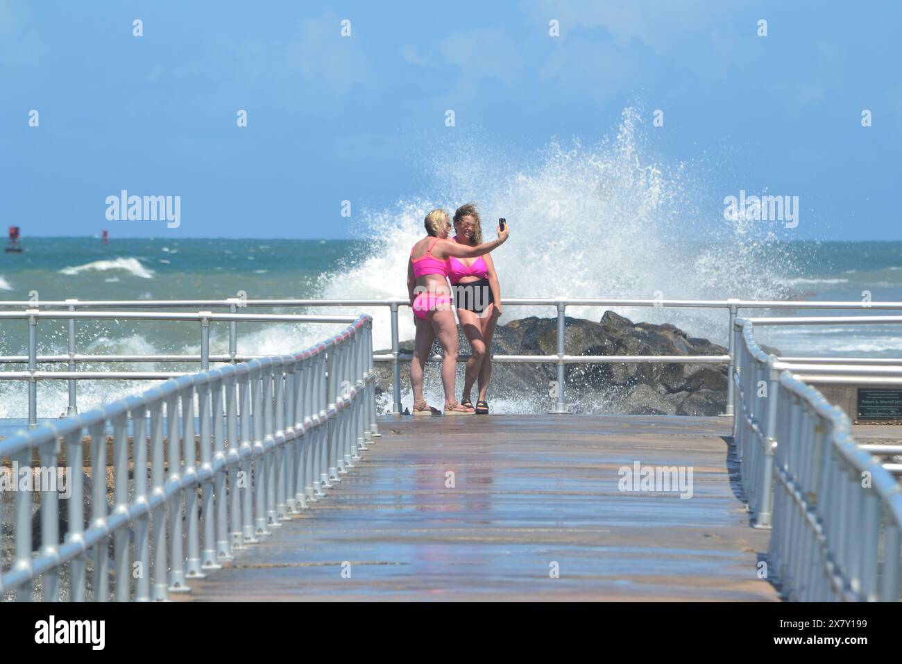 Two women are standing on the concrete jetty pier, capturing a selfie ...