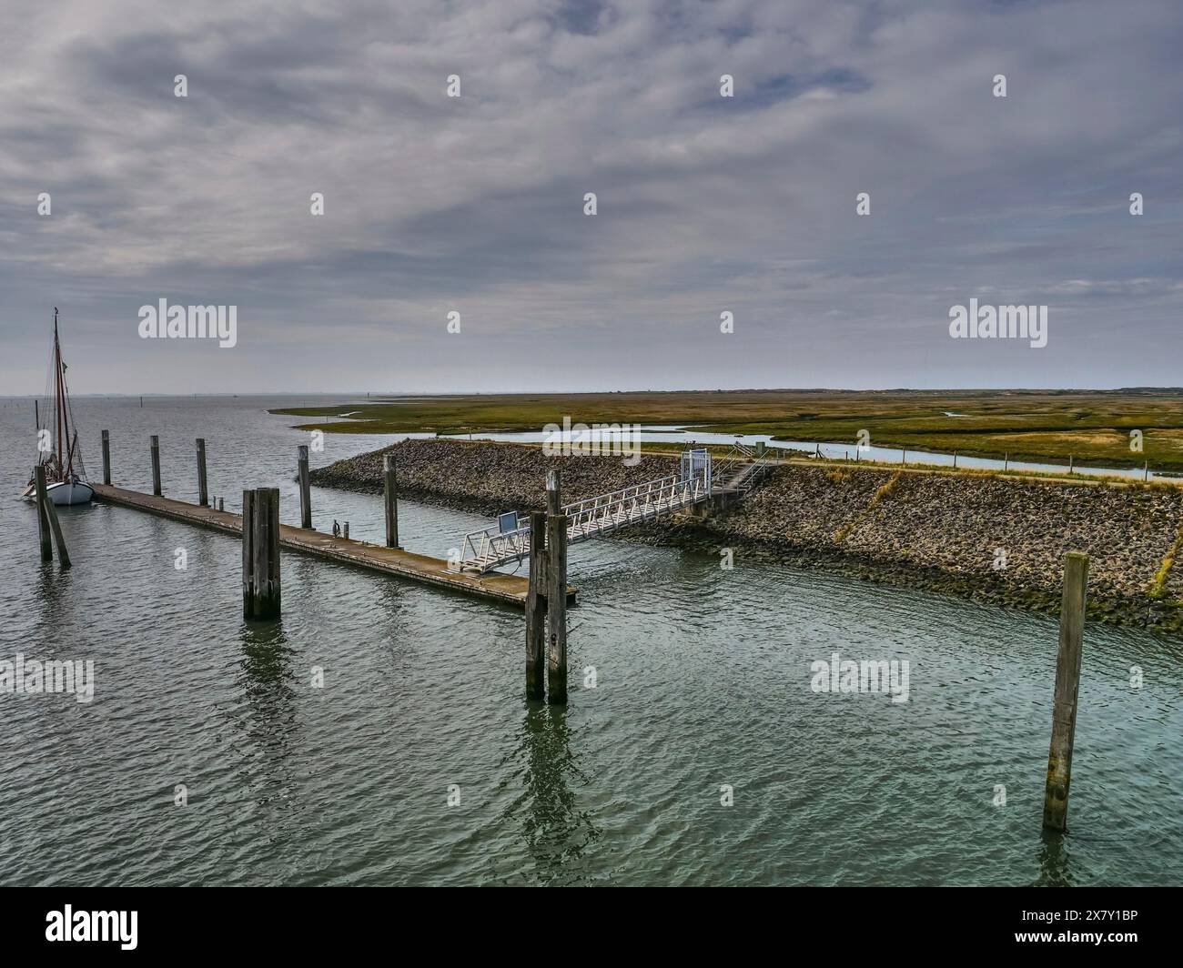 A sailboat, coastal landscape and long jetty under a cloudy sky, small ...