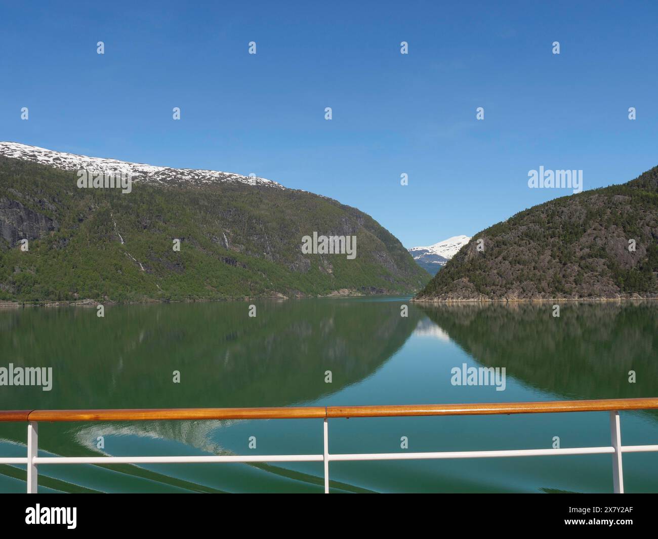 A lake with green mountains and snow-capped peaks seen from a boat with ...