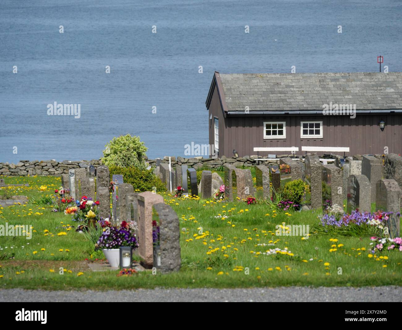 Colourful cemetery with flowers in front of a wooden house on the shore ...