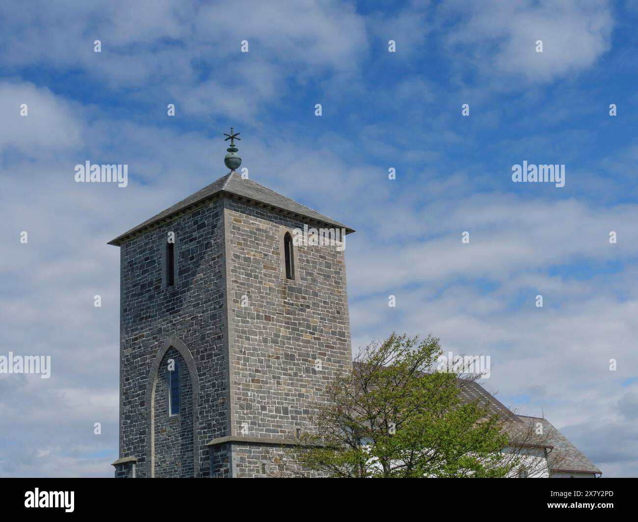 Stony church tower in front of a clear sky, partly hidden by a tree ...