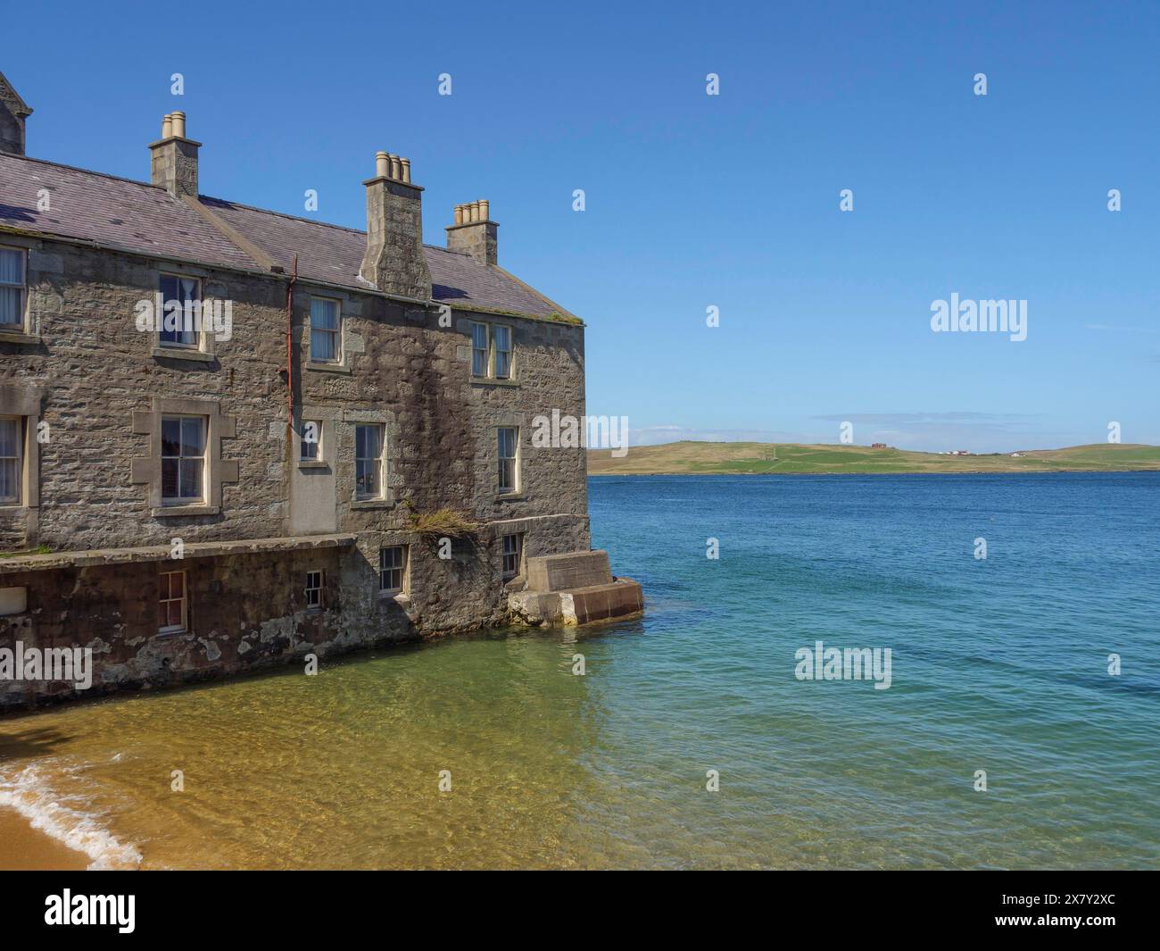 Old stone building near a sandy beach with clear blue water and blue ...