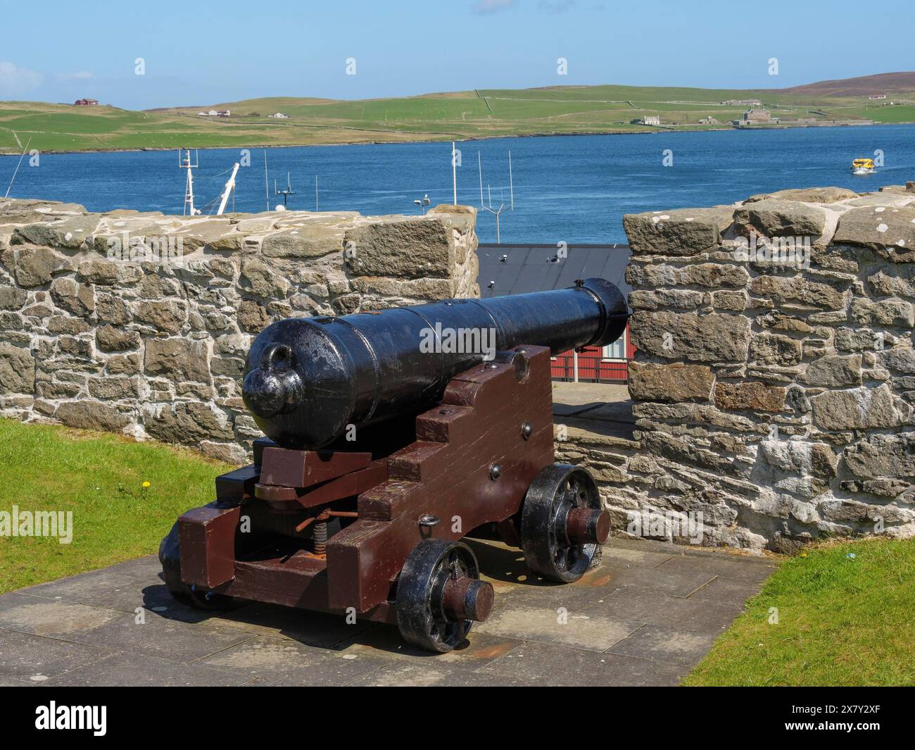 Old cannon in front of a stone wall with a view of the sea and green ...
