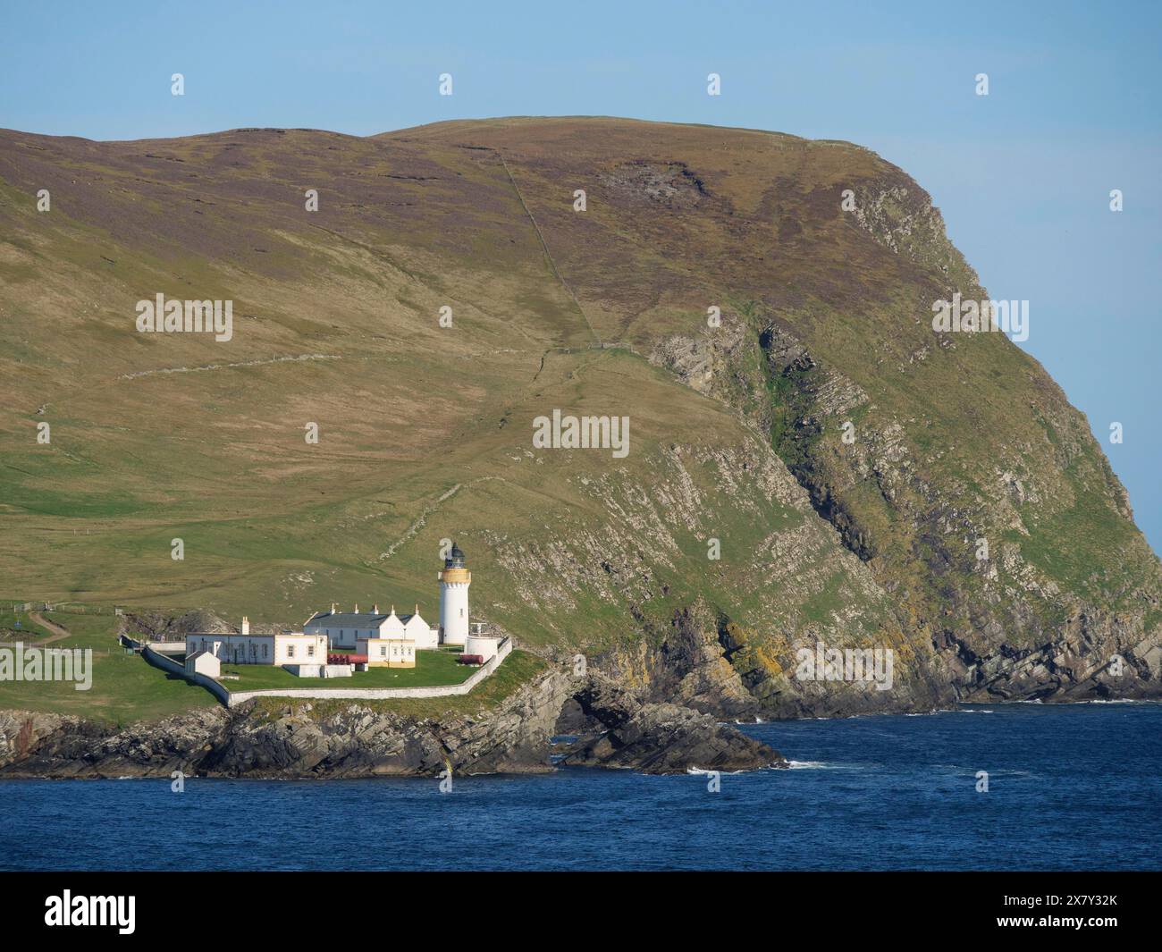 A lighthouse and some houses stand on cliffs on the coast, surrounded ...