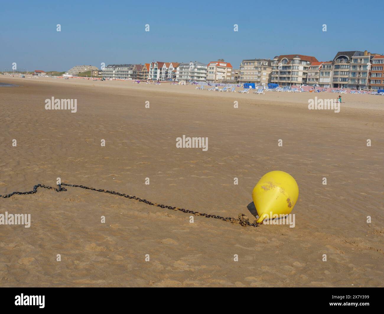 A yellow buoy is attached to the sandy beach with a chain, in front of ...