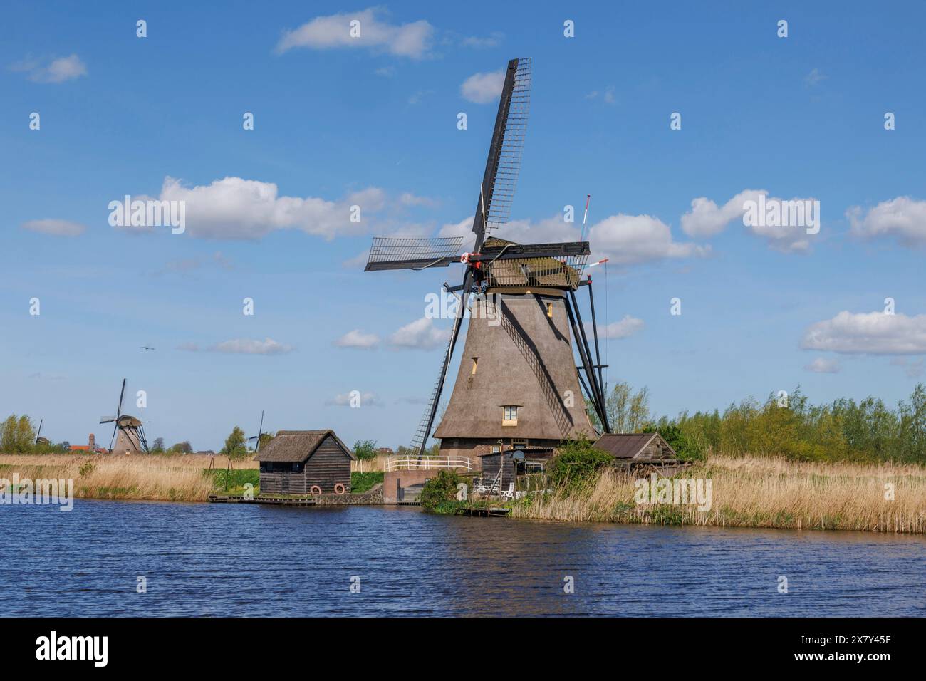 Windmill and buildings on a body of water under a blue sky with white ...