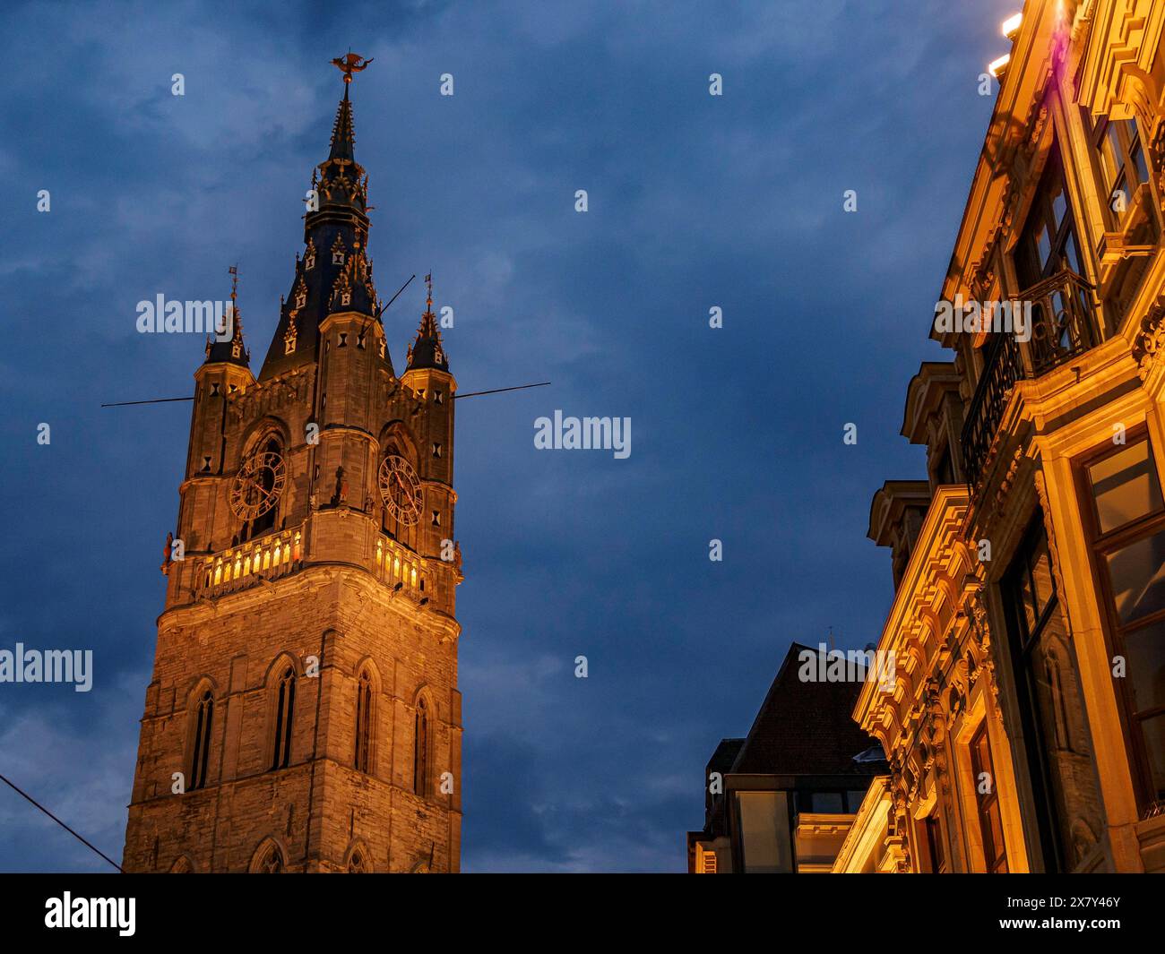 An illuminated Gothic church tower rises into the cloudy night sky of a ...