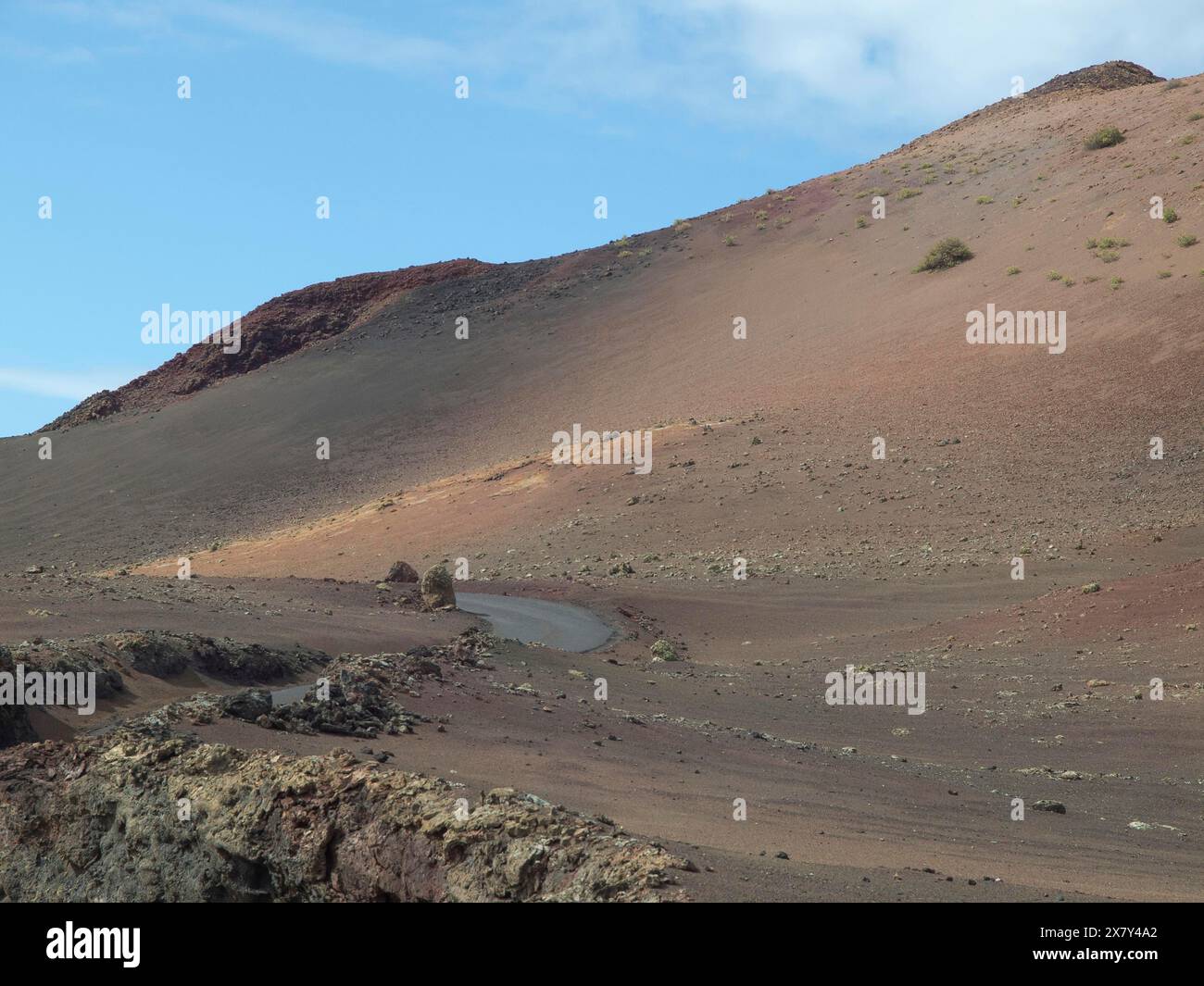 A rocky volcano with a narrow road, surrounded by lava and ash under a ...