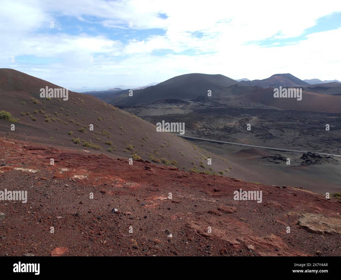 Volcanic landscape with red soil and hills under a slightly cloudy sky ...