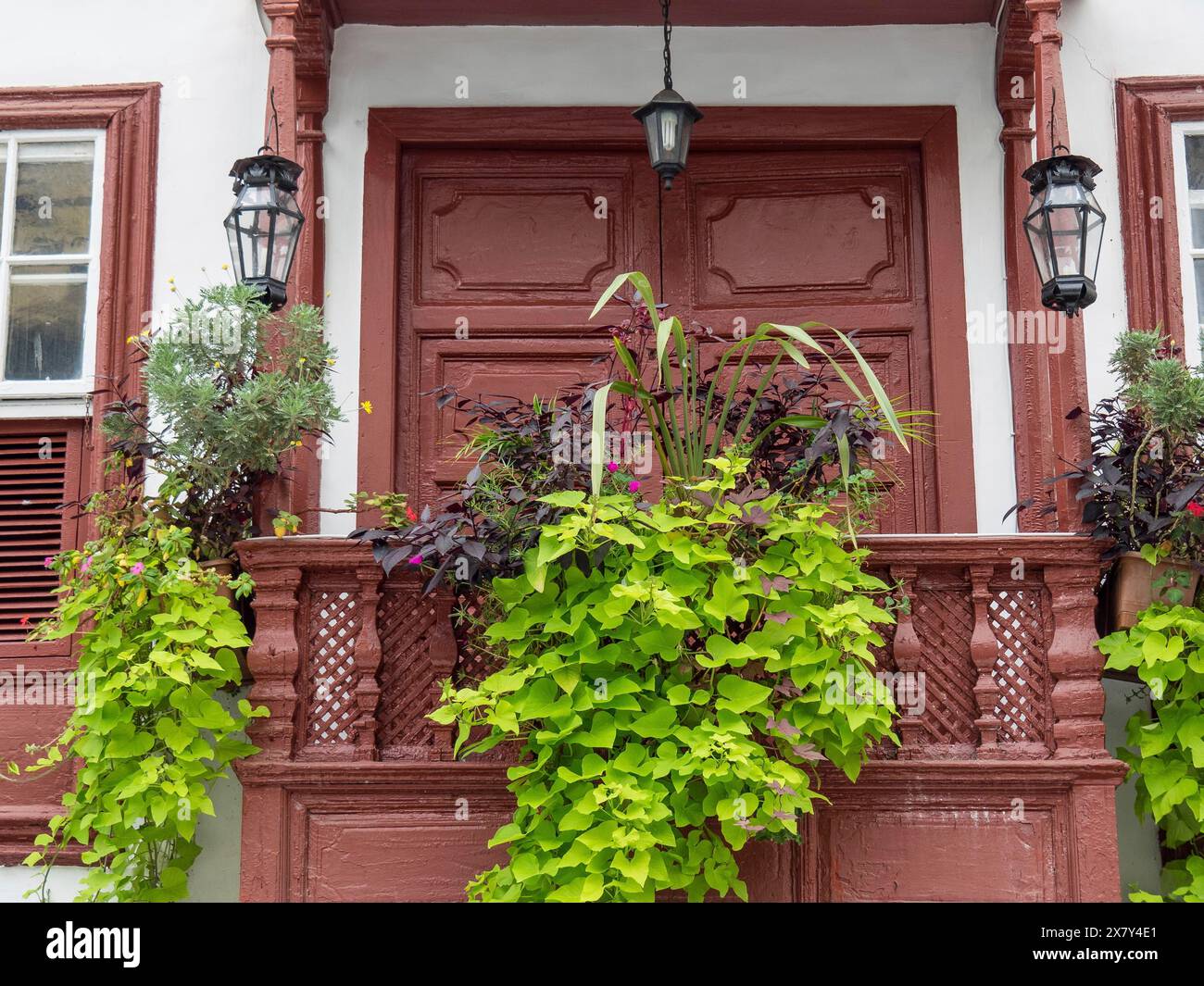 Colonial balcony in red with decorative lanterns and plants adding lush ...