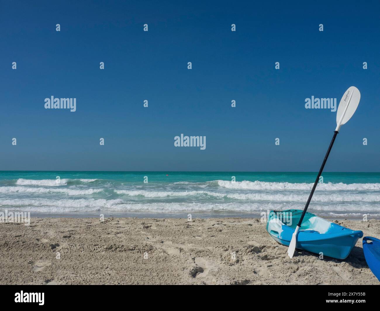 Blue kayak with paddle lies on sandy beach surrounded by gentle waves ...