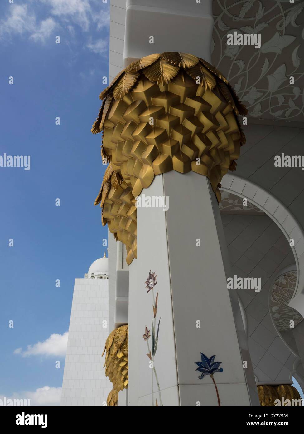 An ornate column with golden leaves against a blue sky, white mosque ...