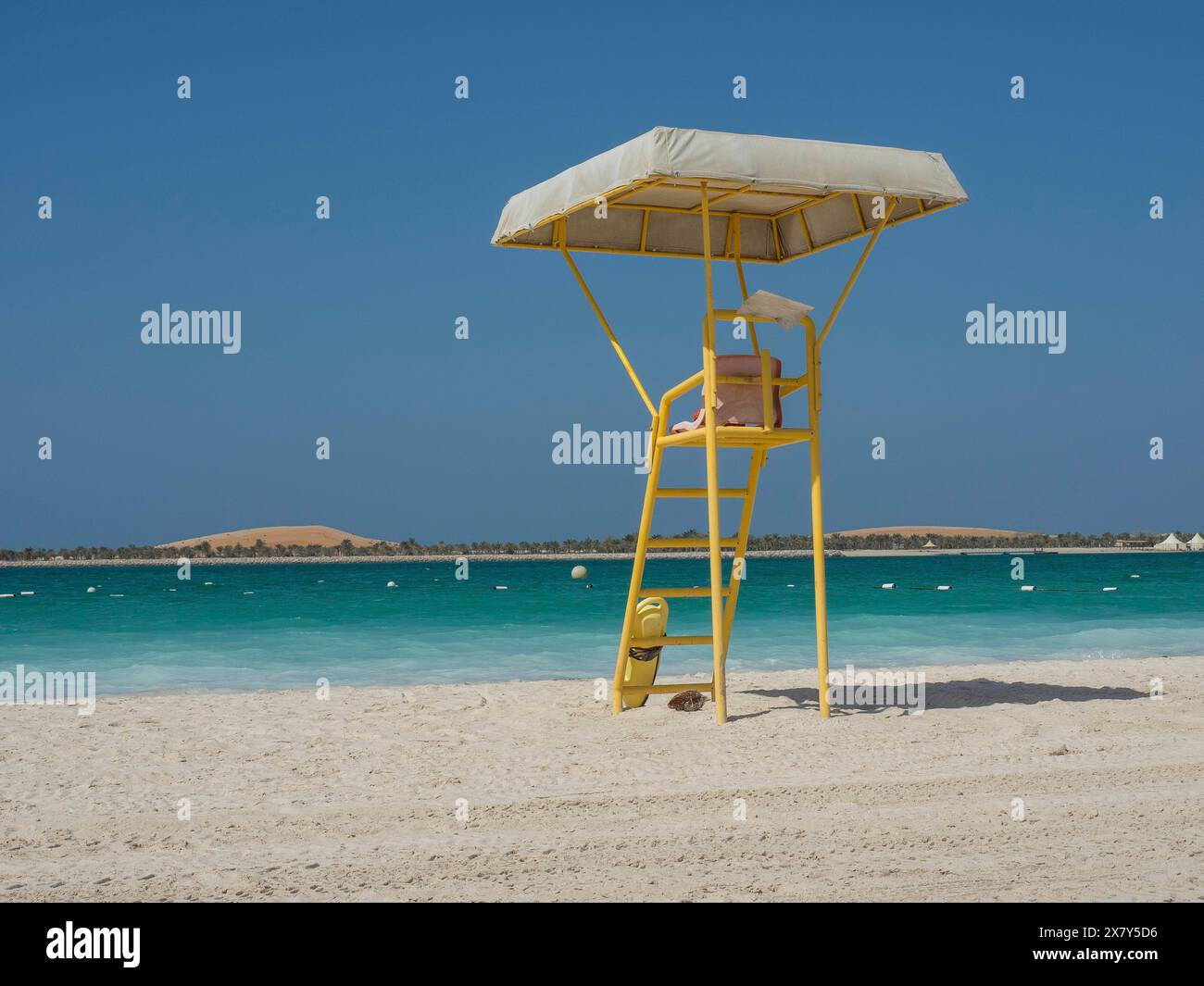 Yellow lifeguard chair on a calm beach with turquoise water and blue ...