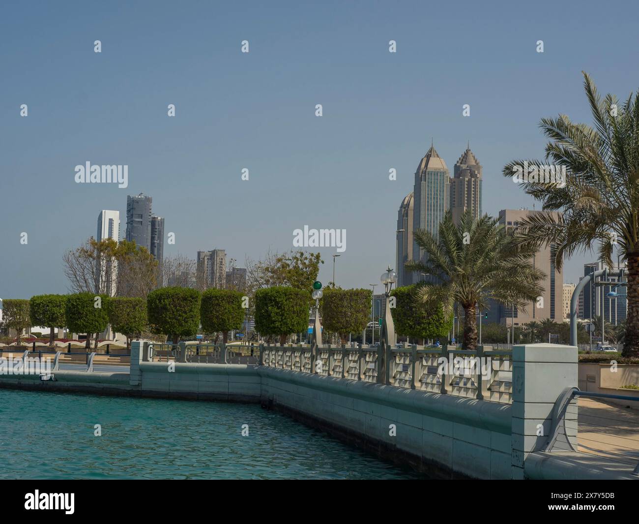 Skyscrapers and palm trees along a seafront promenade in clear, sunny ...