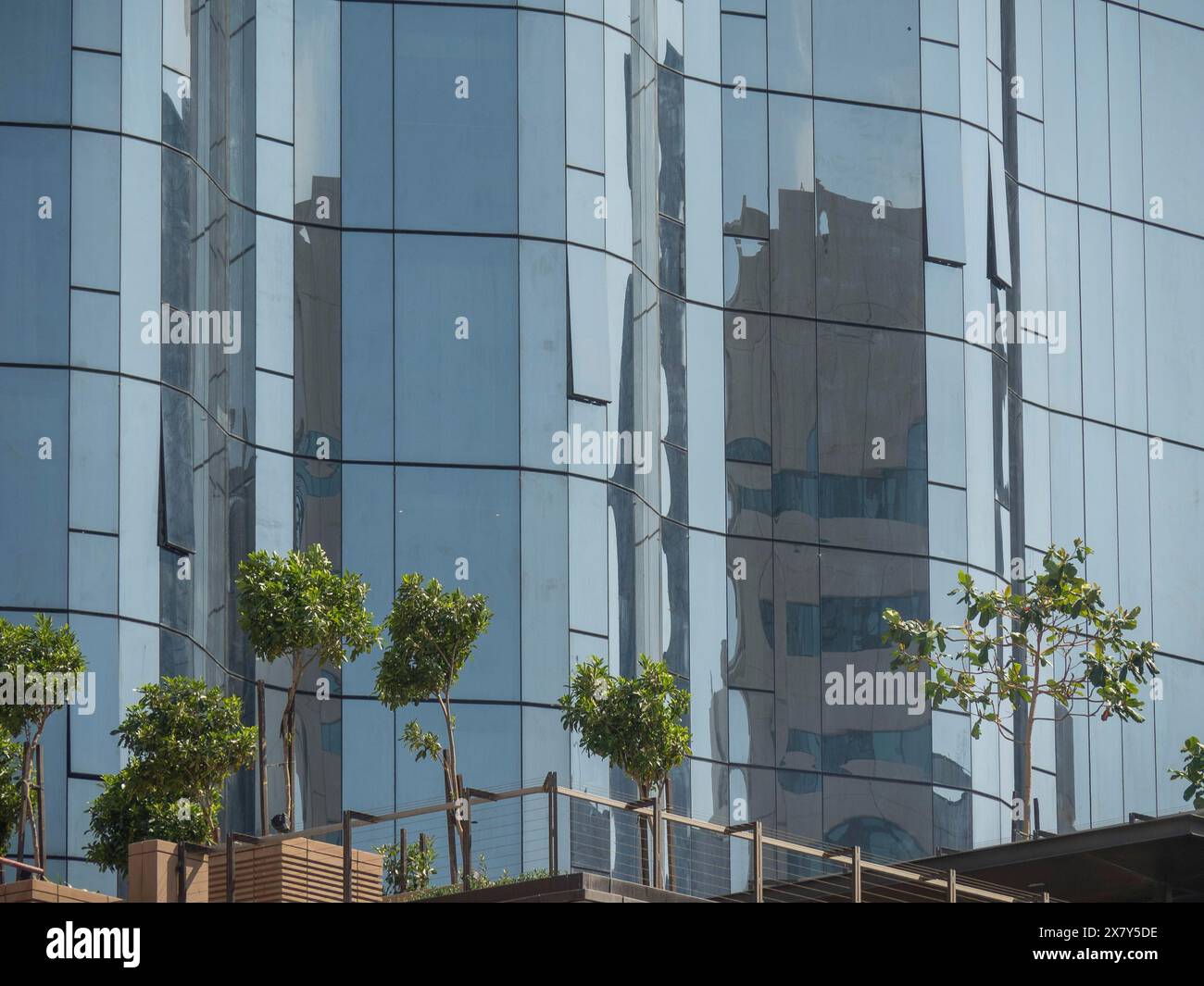 Modern glass façade reflecting other buildings, small trees in front ...