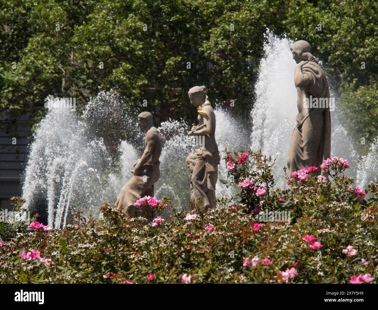 Three statues in a fountain surrounded by blooming flowers and bubbling ...