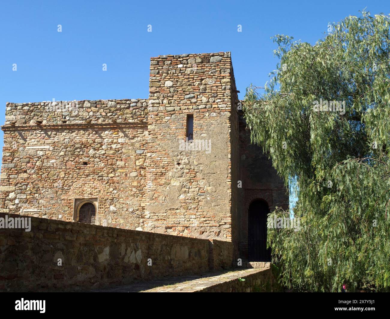 Old building on a stone wall, behind it a tree and a clear blue sky ...