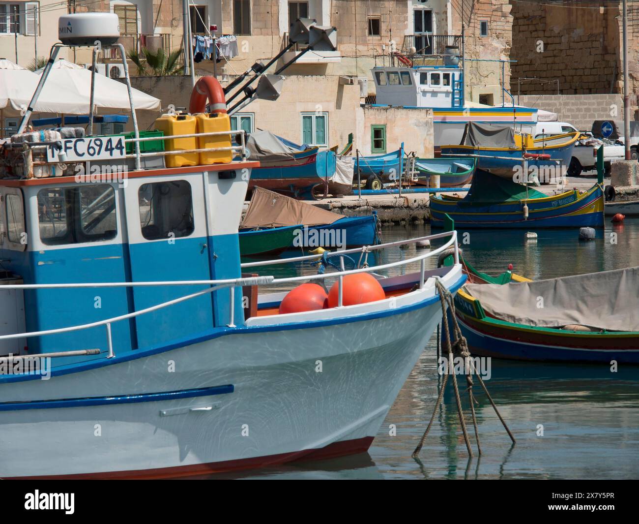 Boats in the harbour of a coastal town with bright colours and adjacent buildings in sunny ...