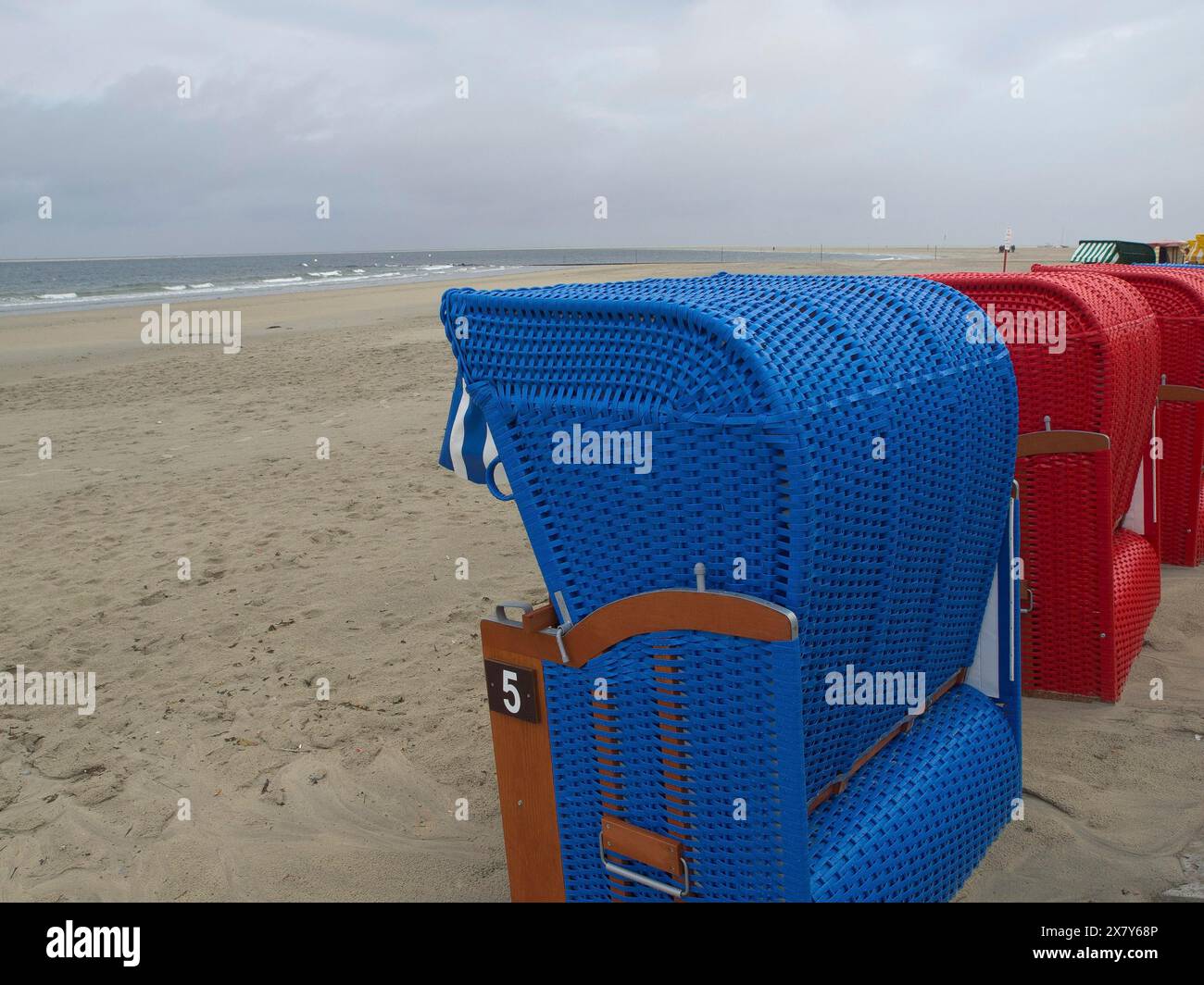 A blue beach chair stands on the beach with other red beach chairs in ...