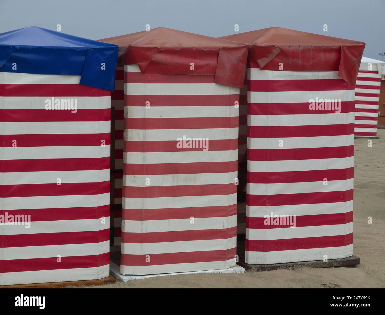 Three colourful beach huts with striped pattern stand on the sandy ...