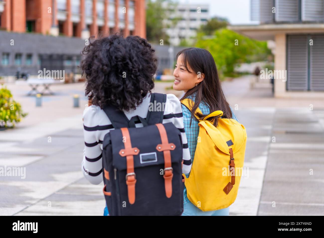 Rear view of two multi-ethnic female students walking along an urban ...