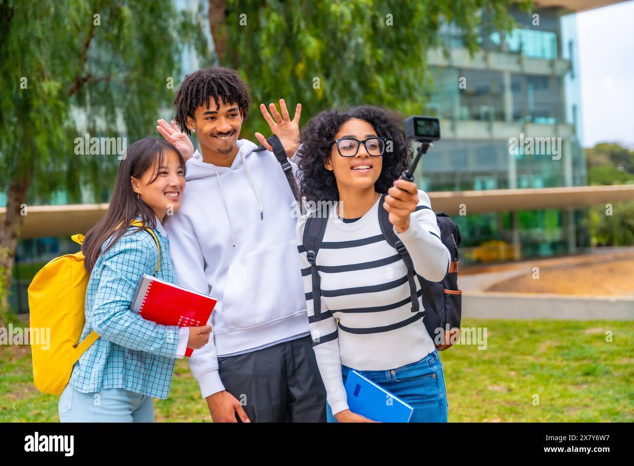 Three multi-ethnic students waving while recording a video with a ...