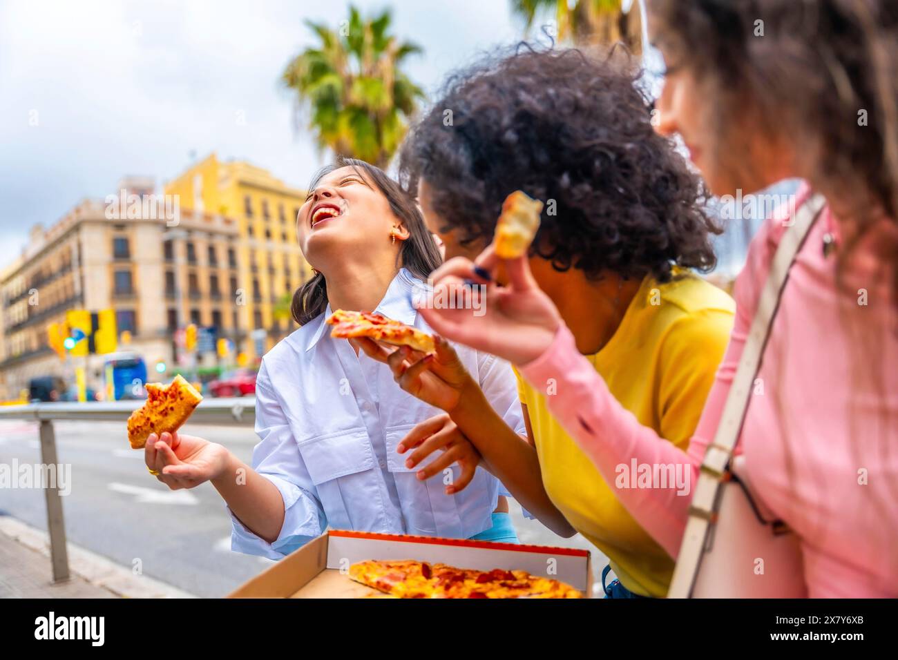Side view of three multiracial women laughing while sharing pizza ...