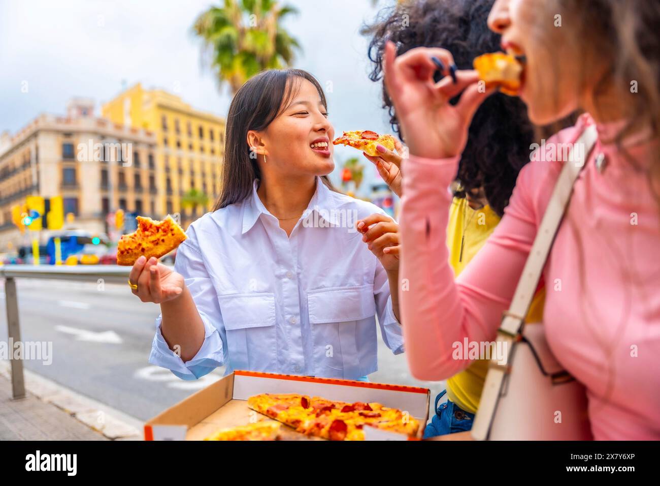 Three multicultural female friends sharing and eating pizza sitting ...