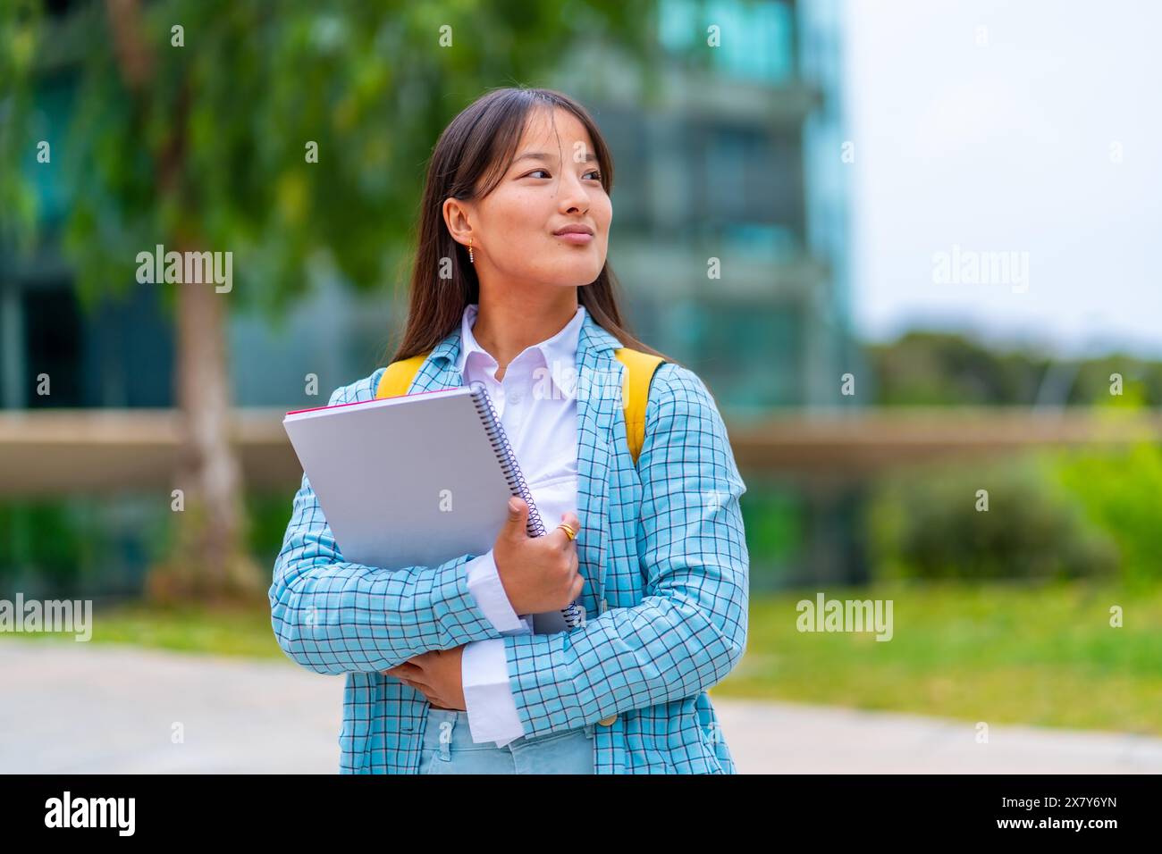 Dreamy chinese student standing outside the university looking away ...