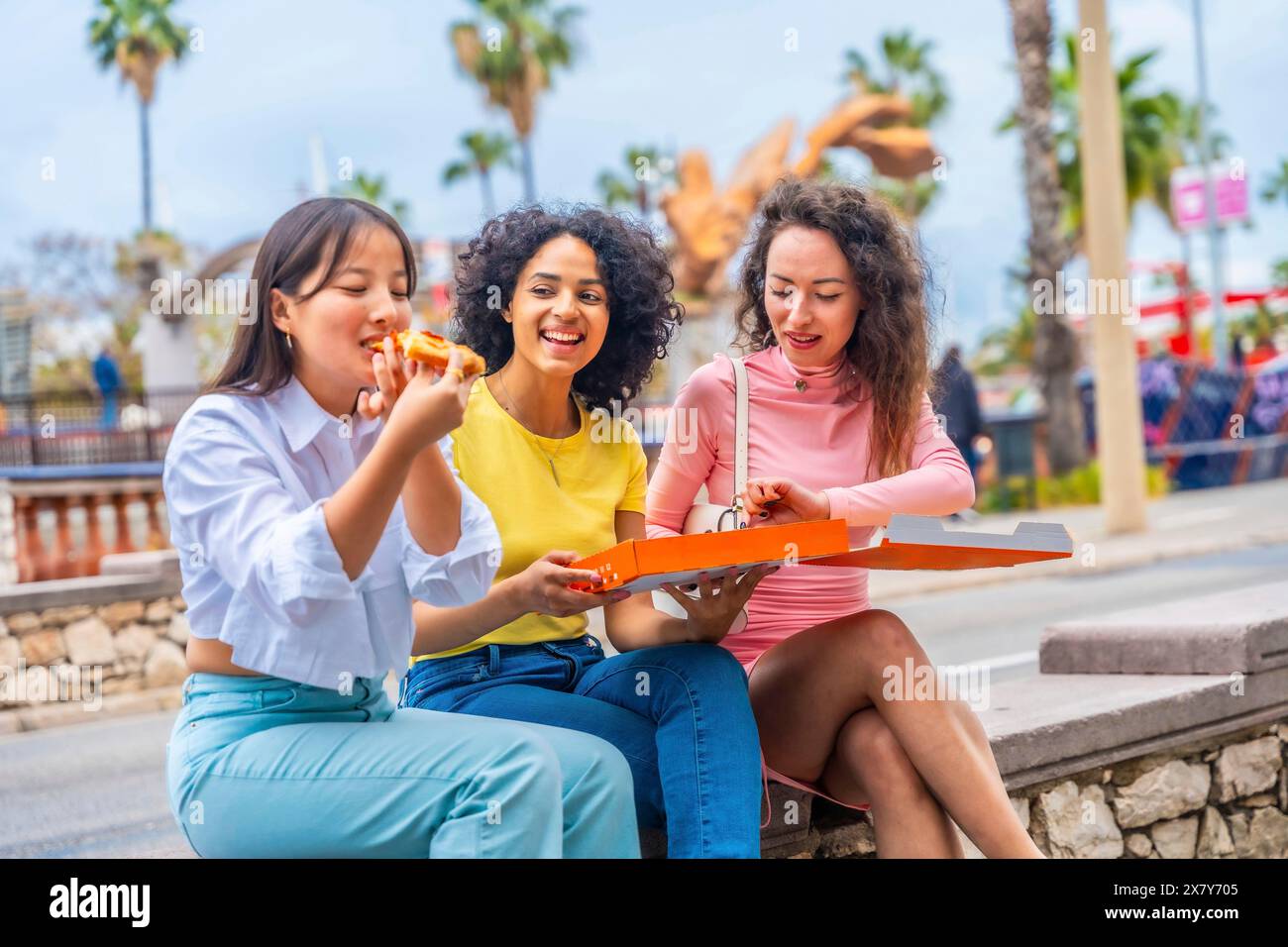 Three female multicultural friends enjoying take away pizza sitting ...