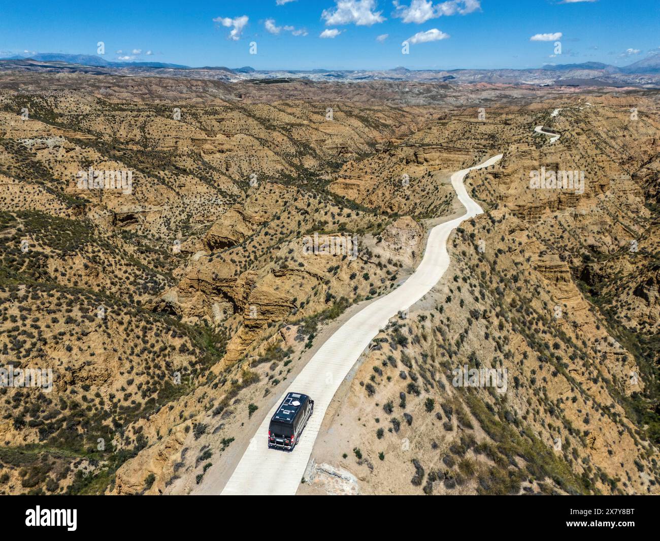 A lonely road leads through barren, hilly desert terrain with a steep ...