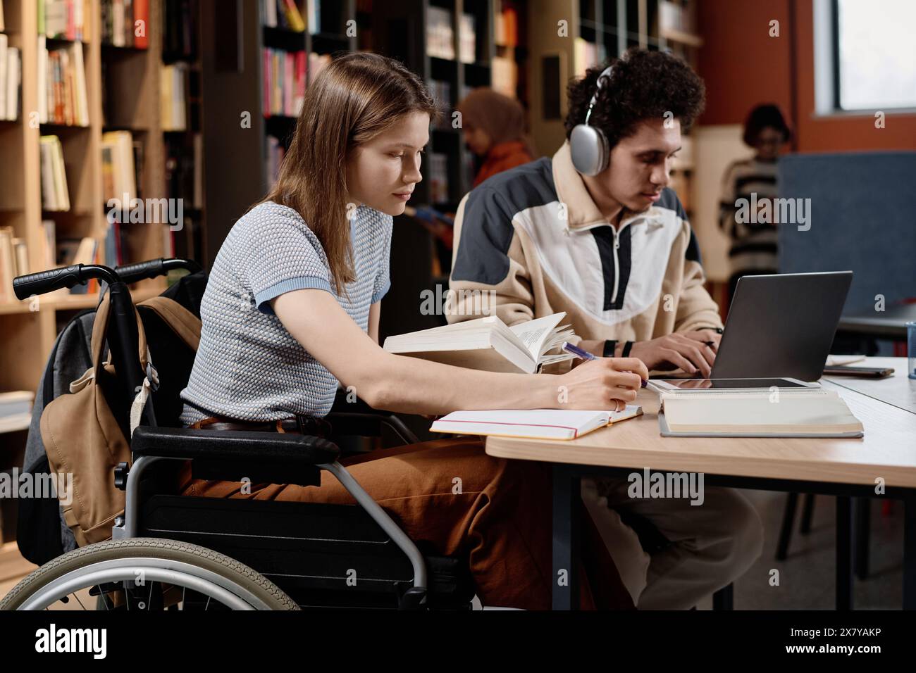 Young female student with disability and her male friend doing homework ...