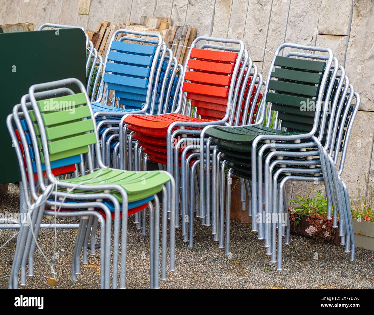 Colorful outdoor chairs stacked on gravel, with wooden slats in green ...