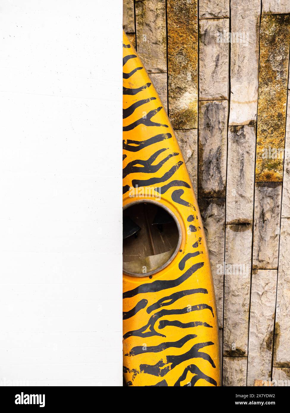A vibrant yellow kayak with black tiger stripes against white and stone ...