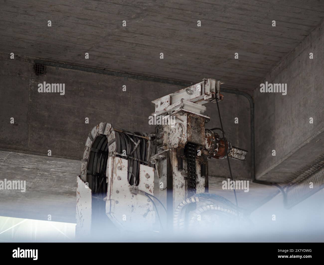 A rusted white industrial machine under a concrete structure. Likely ...