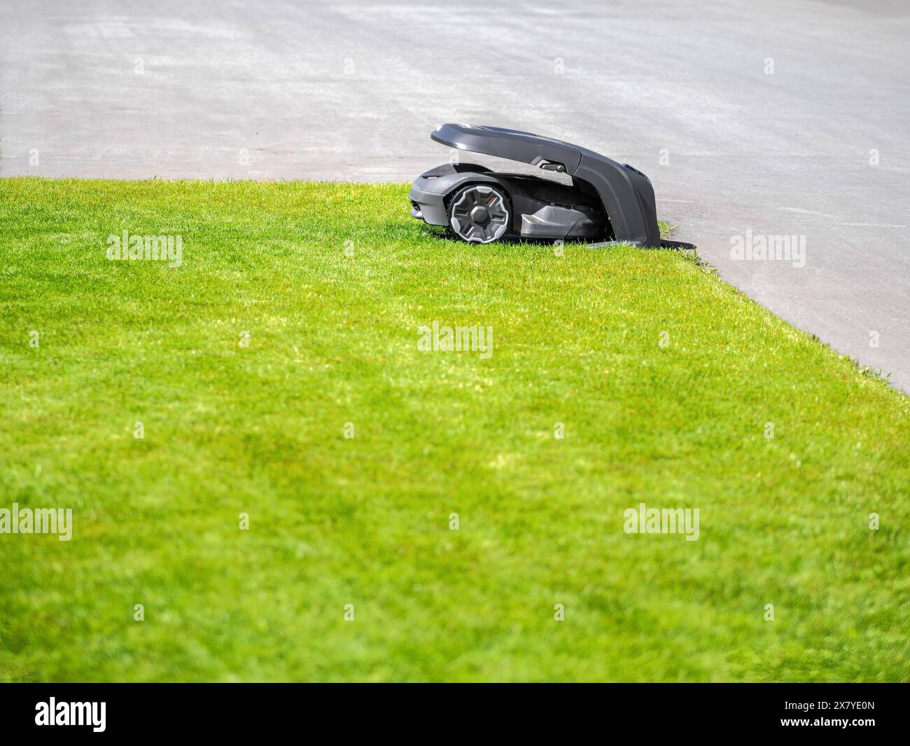 A modern robotic lawn mower on grass and pavement, sleek design, lush ...