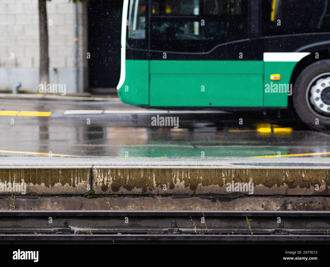 A close-up view of a green bus parked by a curb of tramway rails on a ...