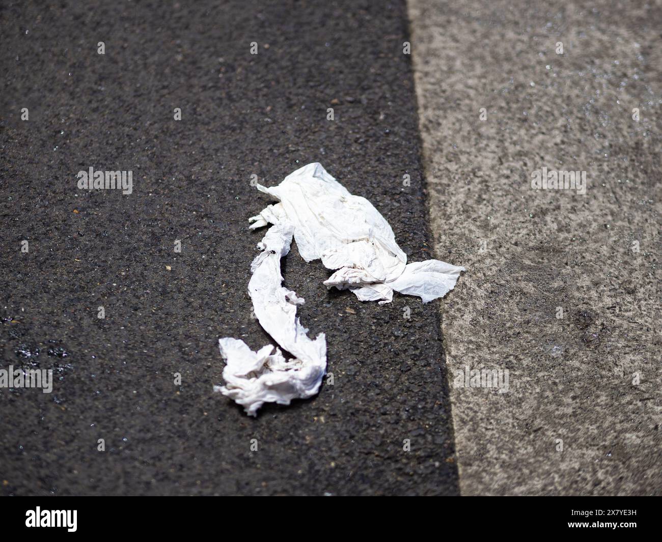 A crumpled tissue lies on the asphalt-concrete road edge, creating a ...