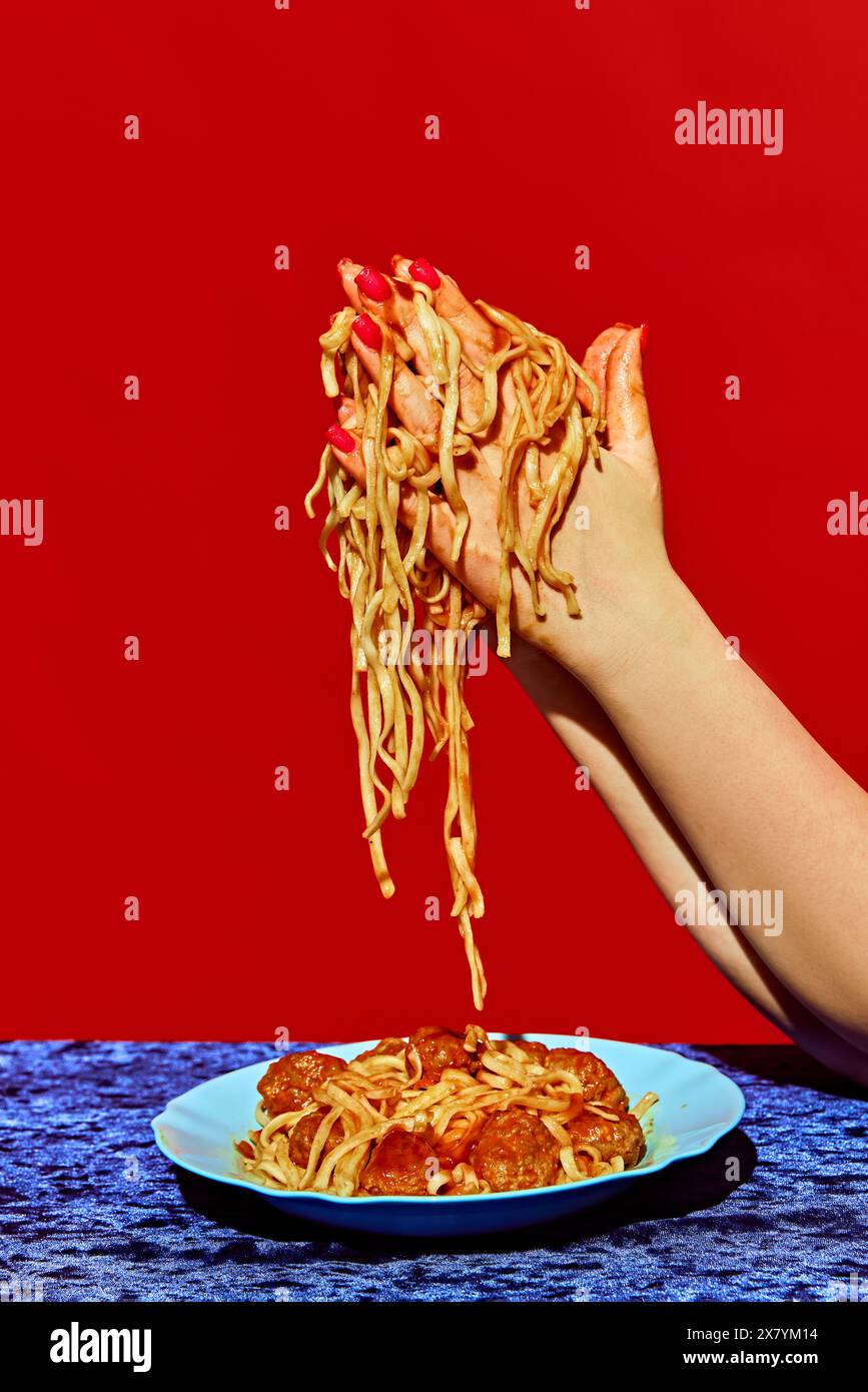 Female hands holding spaghetti with meatballs on plate against red ...