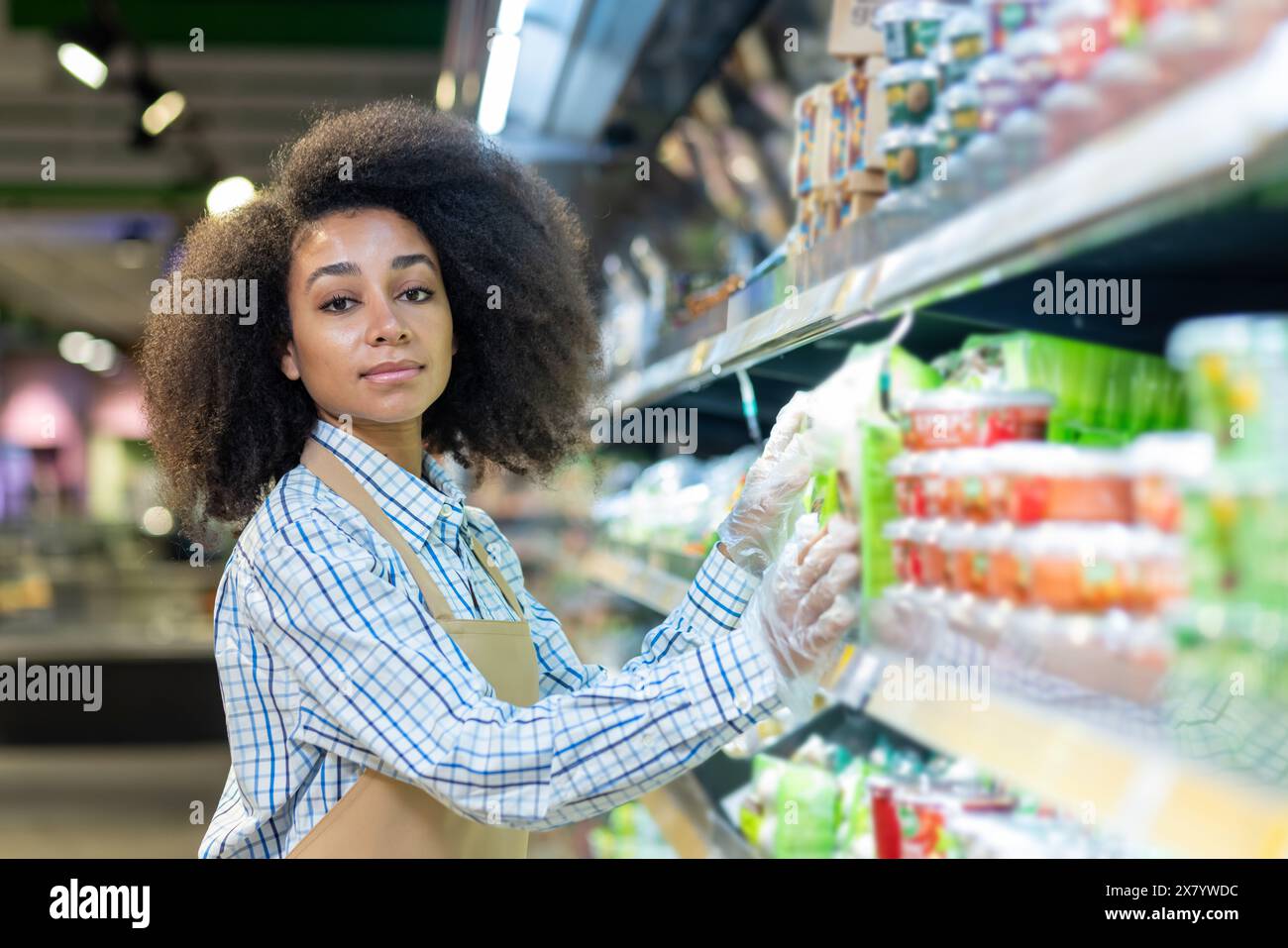 In a welllit supermarket aisle, a dedicated female employee with curly ...