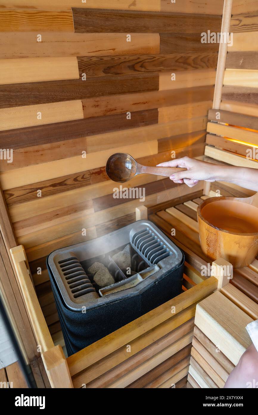 Woman pouring water onto hot stone in sauna room. Steam from water on ...
