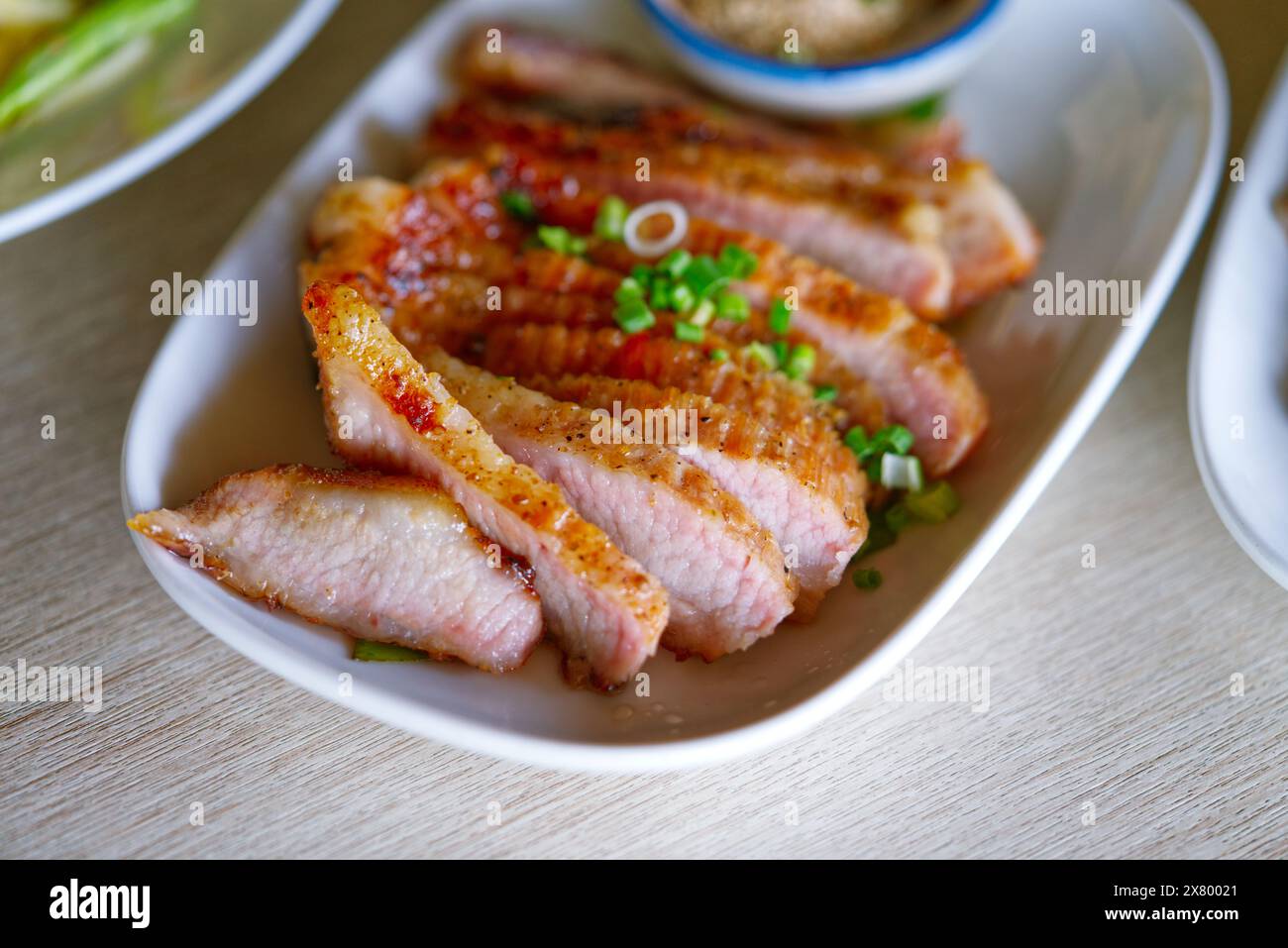 Grilled sliced pig neck in white plate with natural light, popular ...
